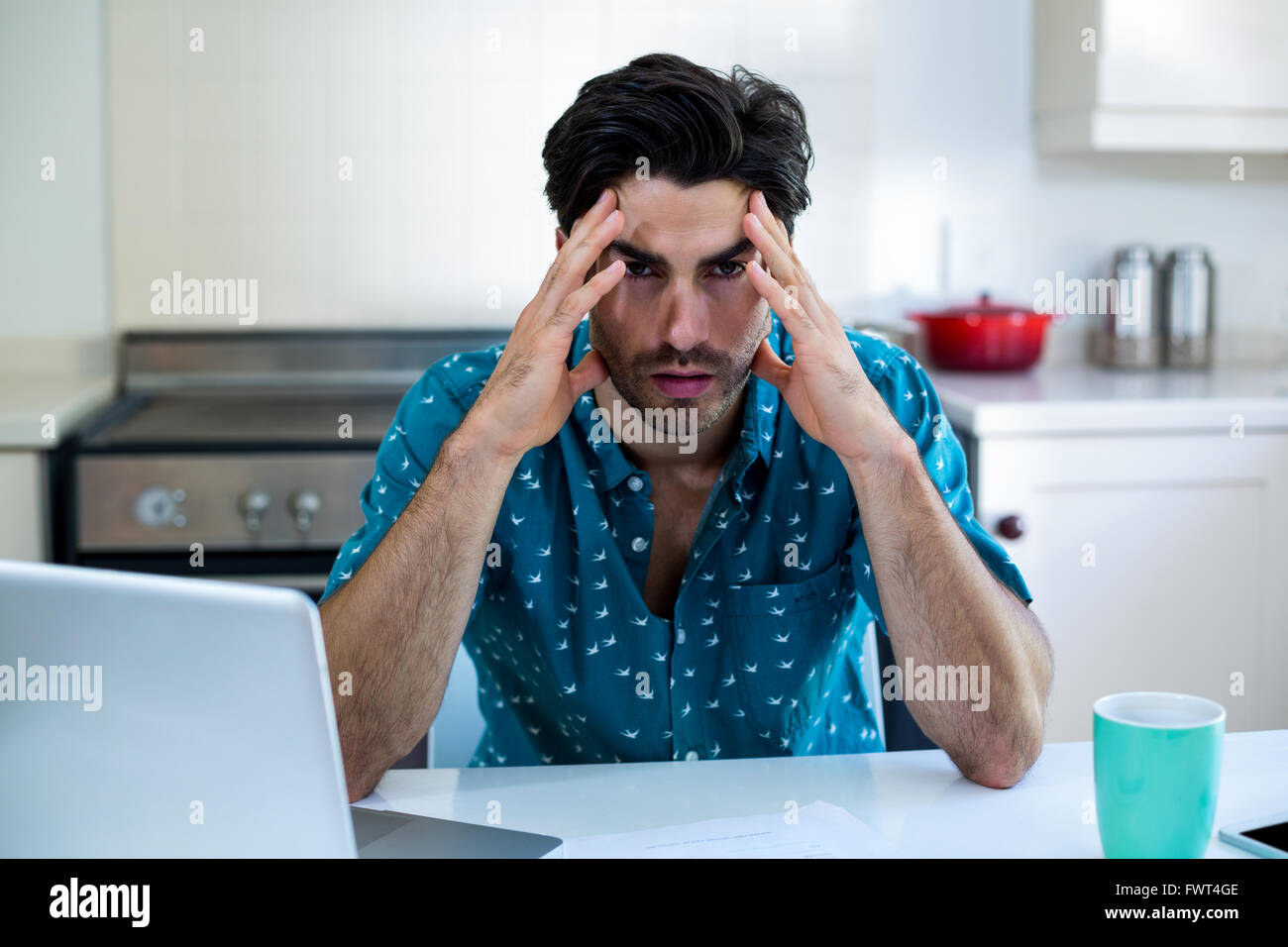 Tensed man sitting with bills and laptop in kitchen Stock Photo - Alamy