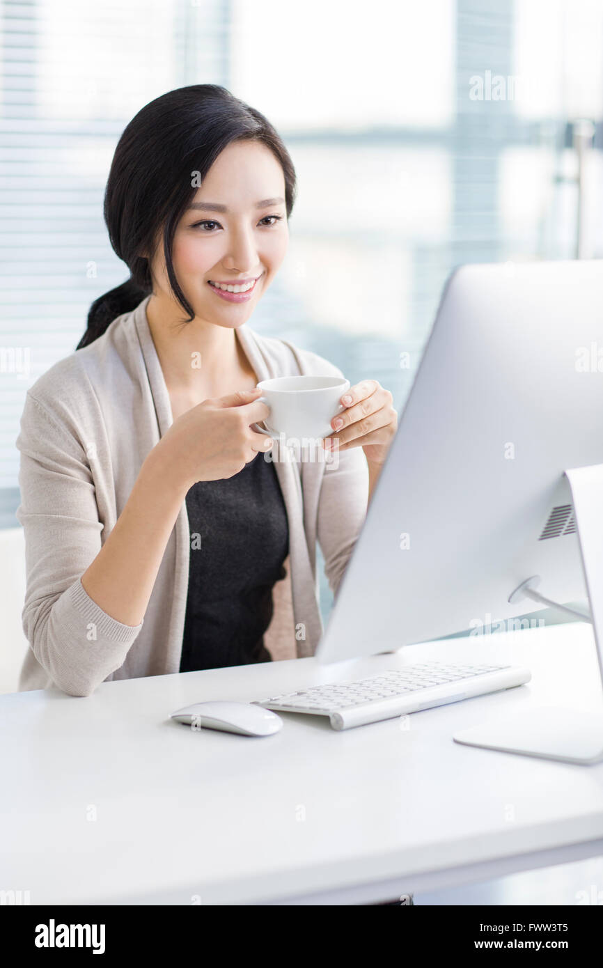 Young woman drinking coffee in office Stock Photo - Alamy