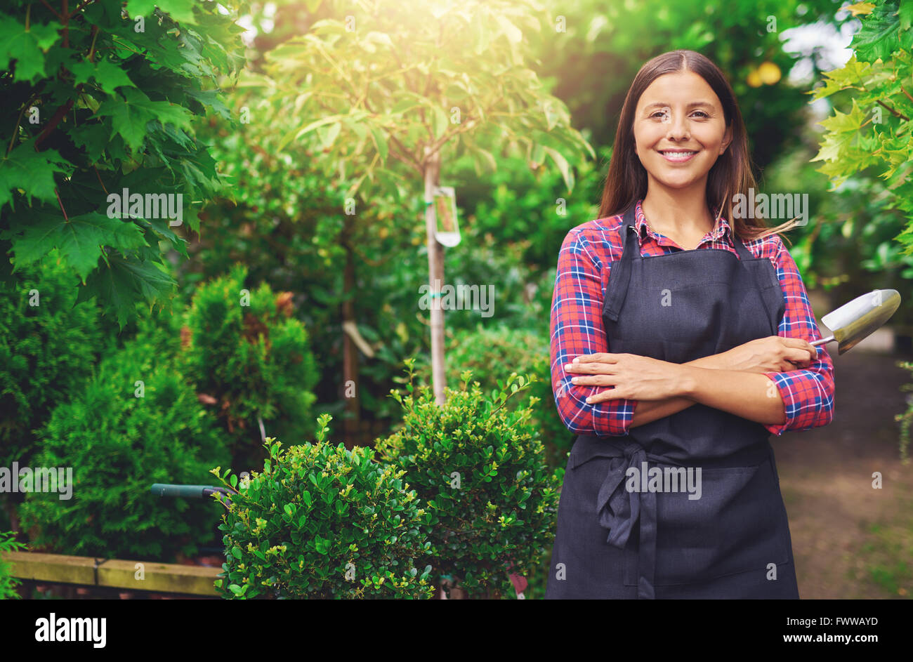 Happy attractive young female botanist working at a nursery standing in ...