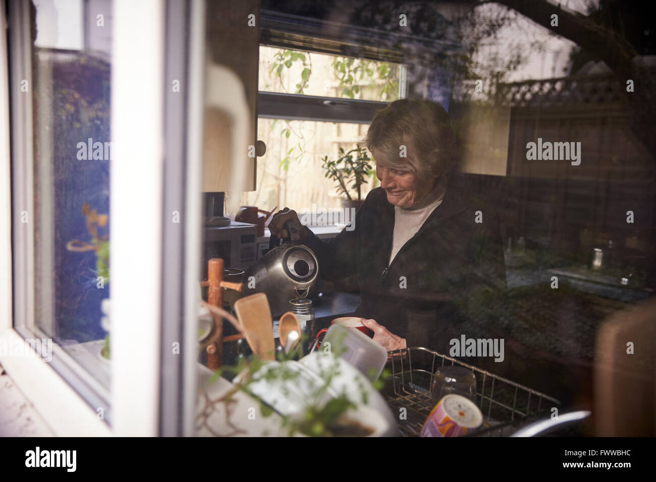 Senior Woman Making Hot Drink In Kitchen Shot Through Window Stock ...