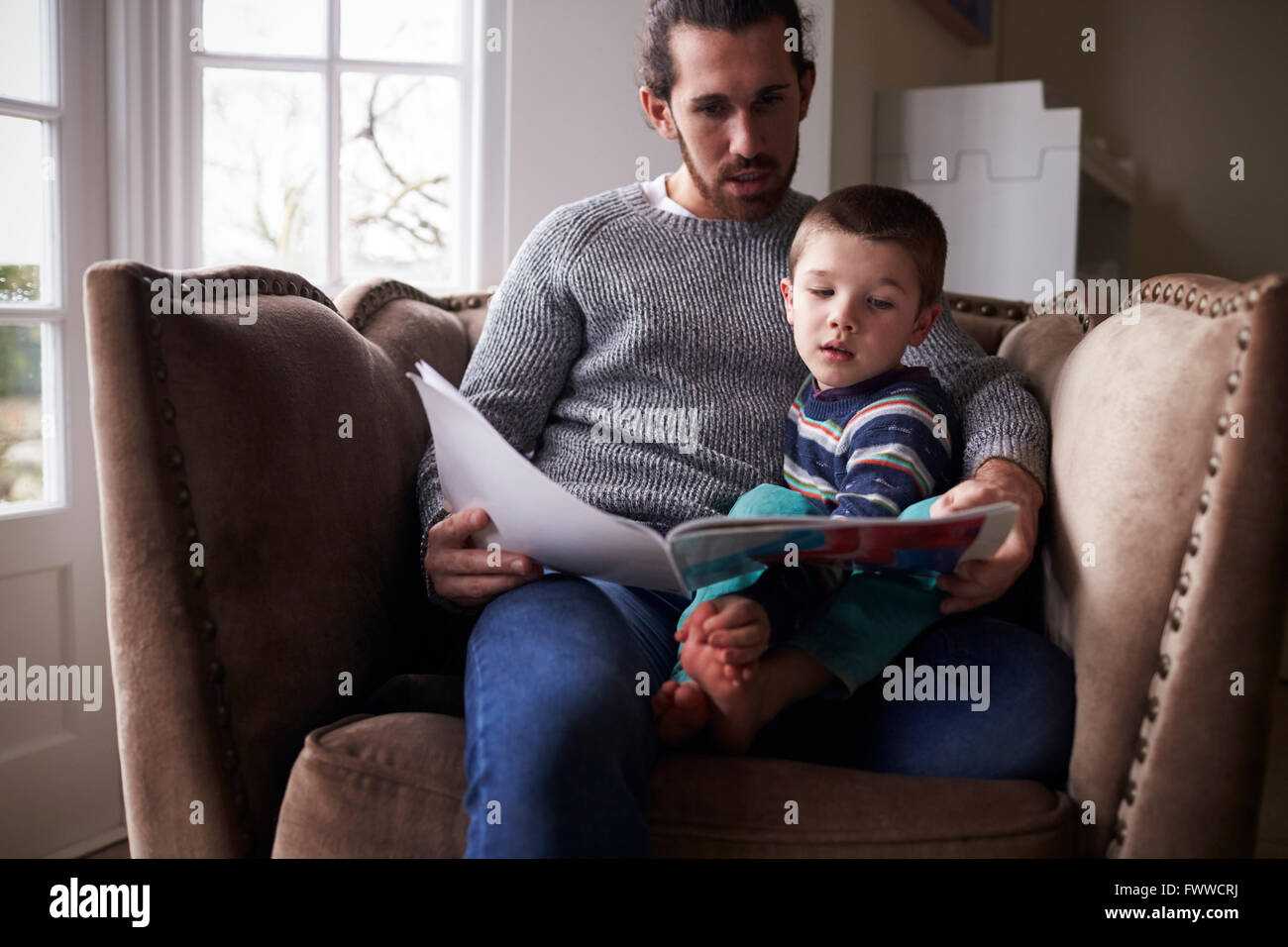 Father Sitting In Chair At Home Reading Story To Son Stock Photo - Alamy