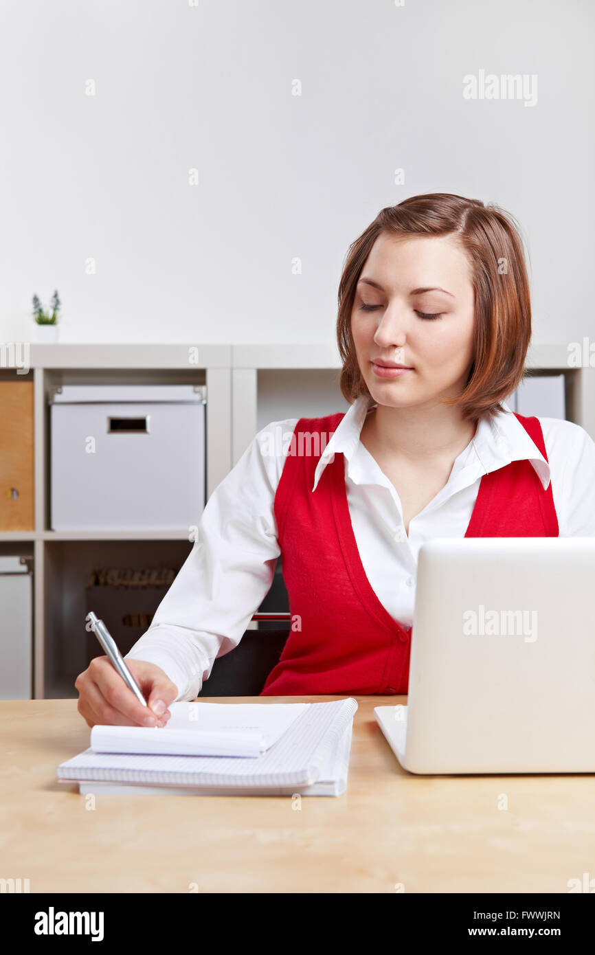 Businesswoman with computer taking notes at her desk in the office ...
