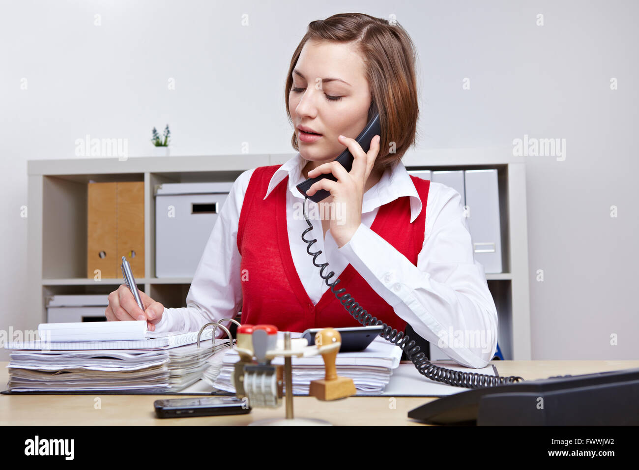 Secretary in business office taking notes while talking on the phone ...