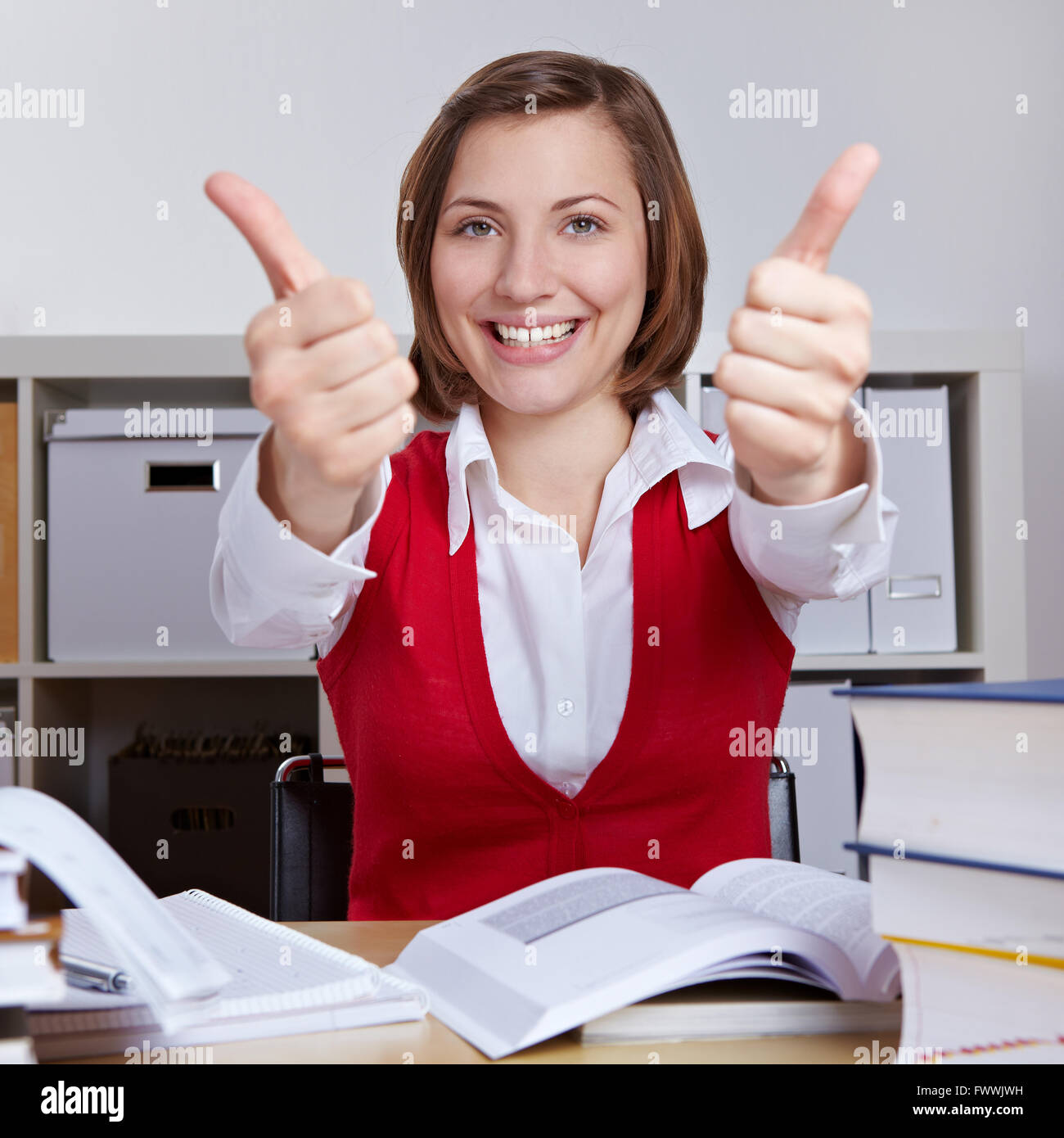 Successful student at desk with books holding both thumbs up Stock ...