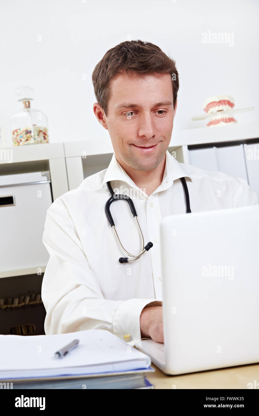 Smiling doctor in his office working on laptop Stock Photo - Alamy