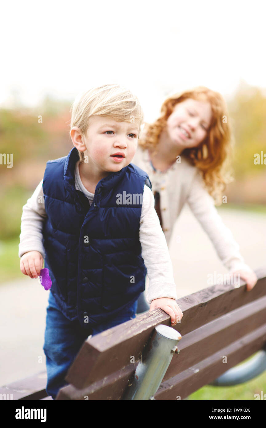 Brother and sister standing on a park bench Stock Photo - Alamy