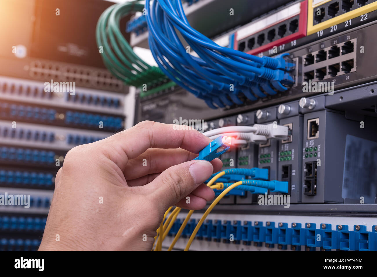 man working in network server room with fiber optic hub for digital ...