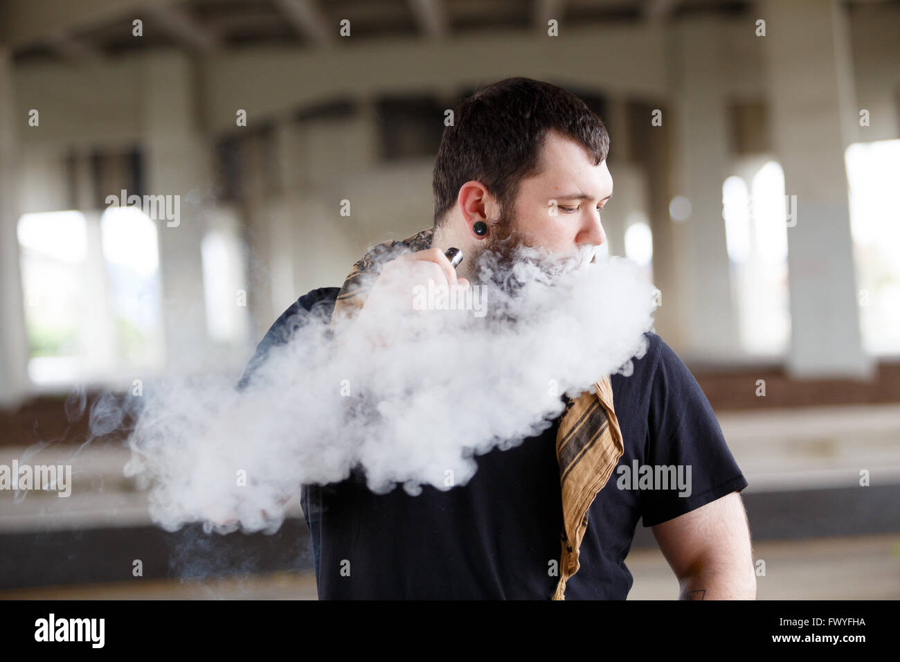 Urban lifestyle portrait of a man vaping in an urban environment with a ...
