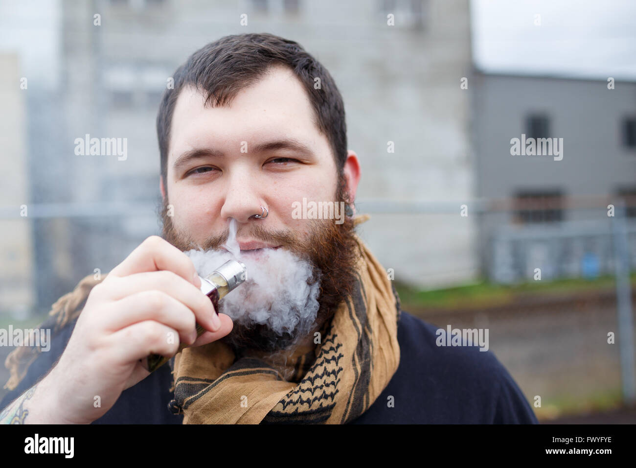 Urban lifestyle portrait of a man vaping in an urban environment with a ...