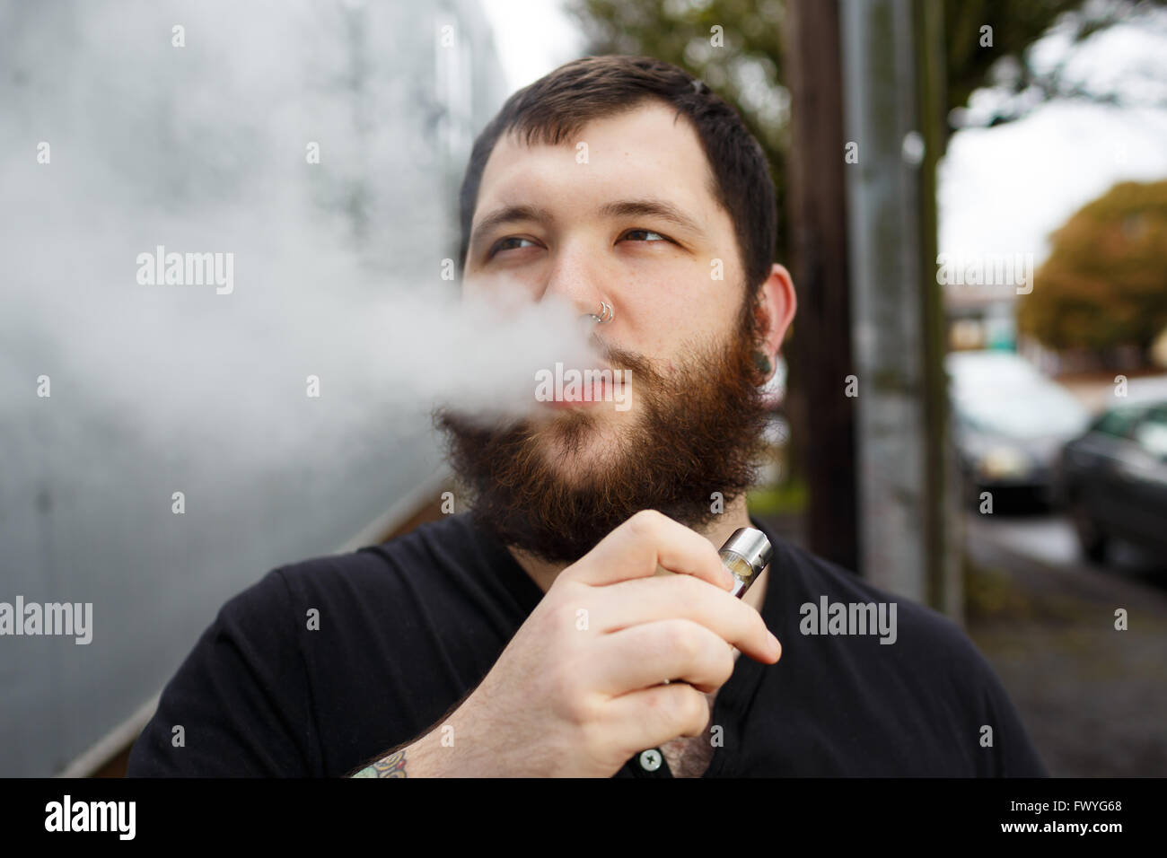 Urban lifestyle portrait of a man vaping in an urban environment with a ...