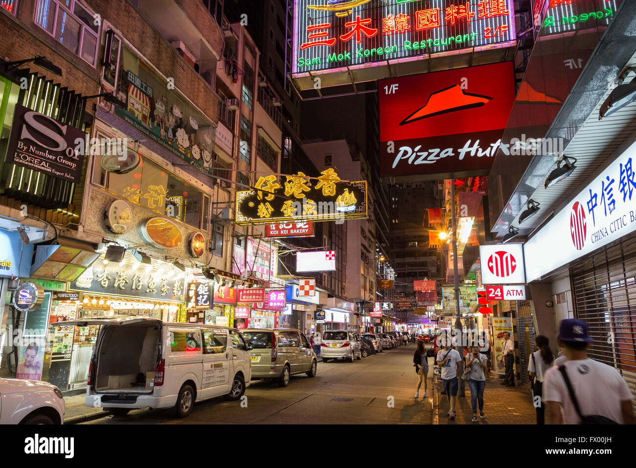 People and cars at a street full of shops and restaurants in Tsim Sha Tsui, Hong Kong, China, at ...