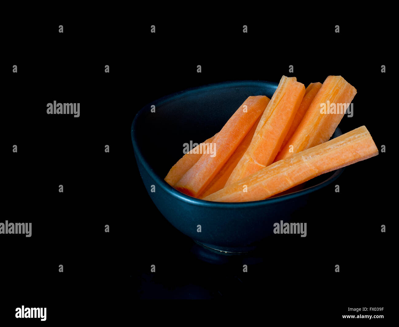 Healthy snack.Fresh cut carrot sticks in dark bowl on black with copy ...