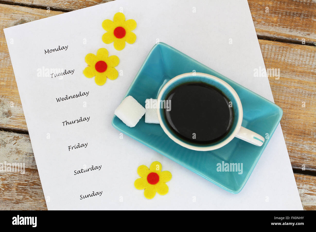 Days of the week listed on white piece of paper, cup of black coffee ...