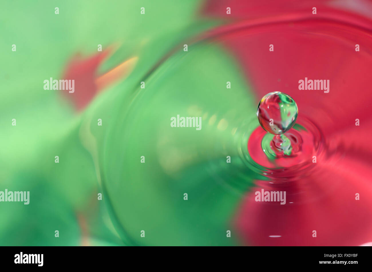 Water drop is falling into the water, red green background Stock Photo ...