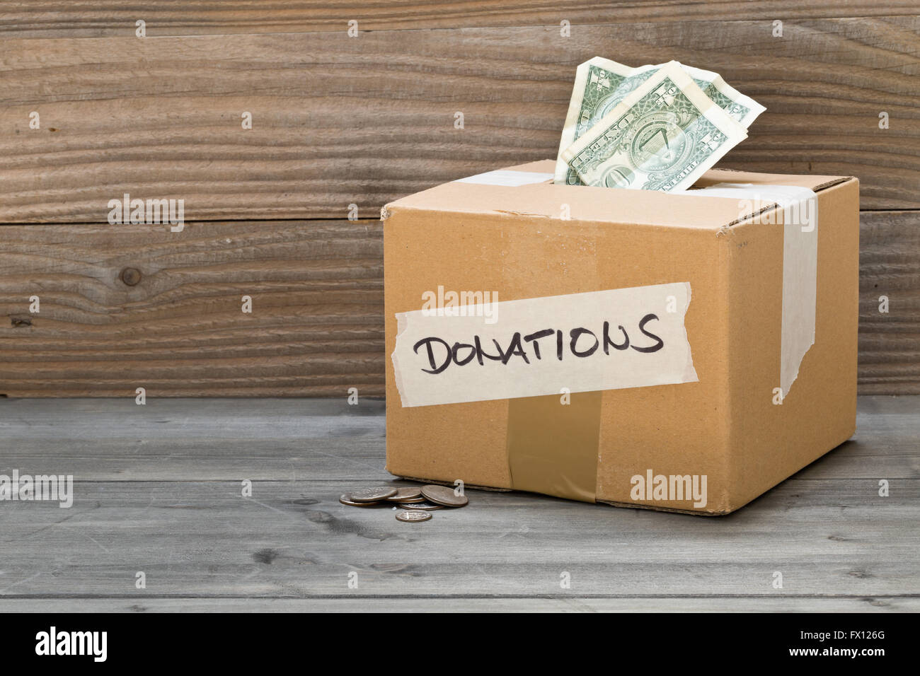 Donation carton box with dollar bills and coins on wooden table ...