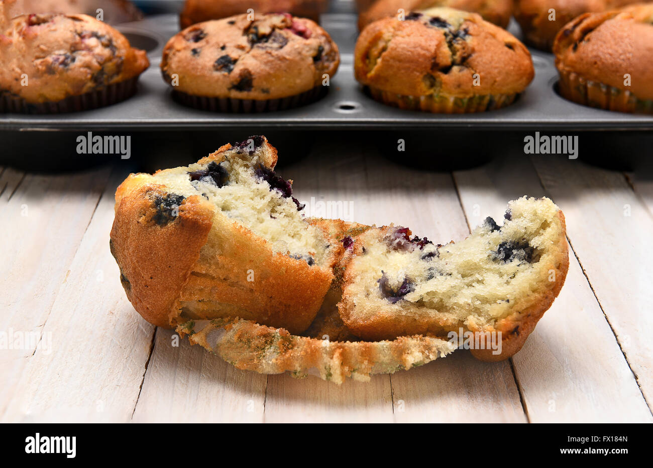A blueberry muffin in front of a pan full of fresh baked muffins ...