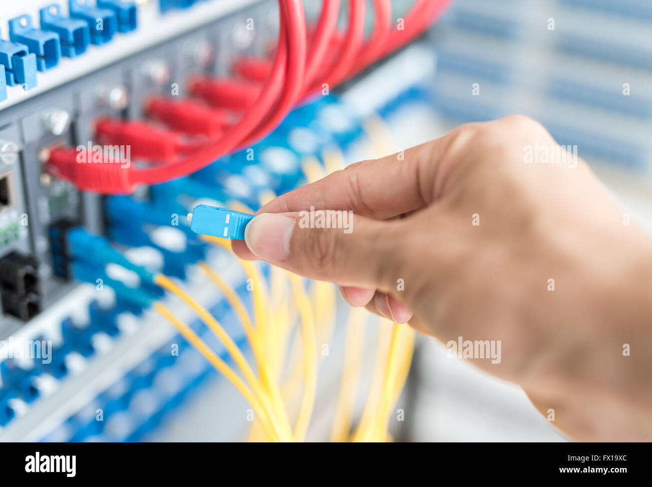 man working in network server room with fiber optic hub for digital ...