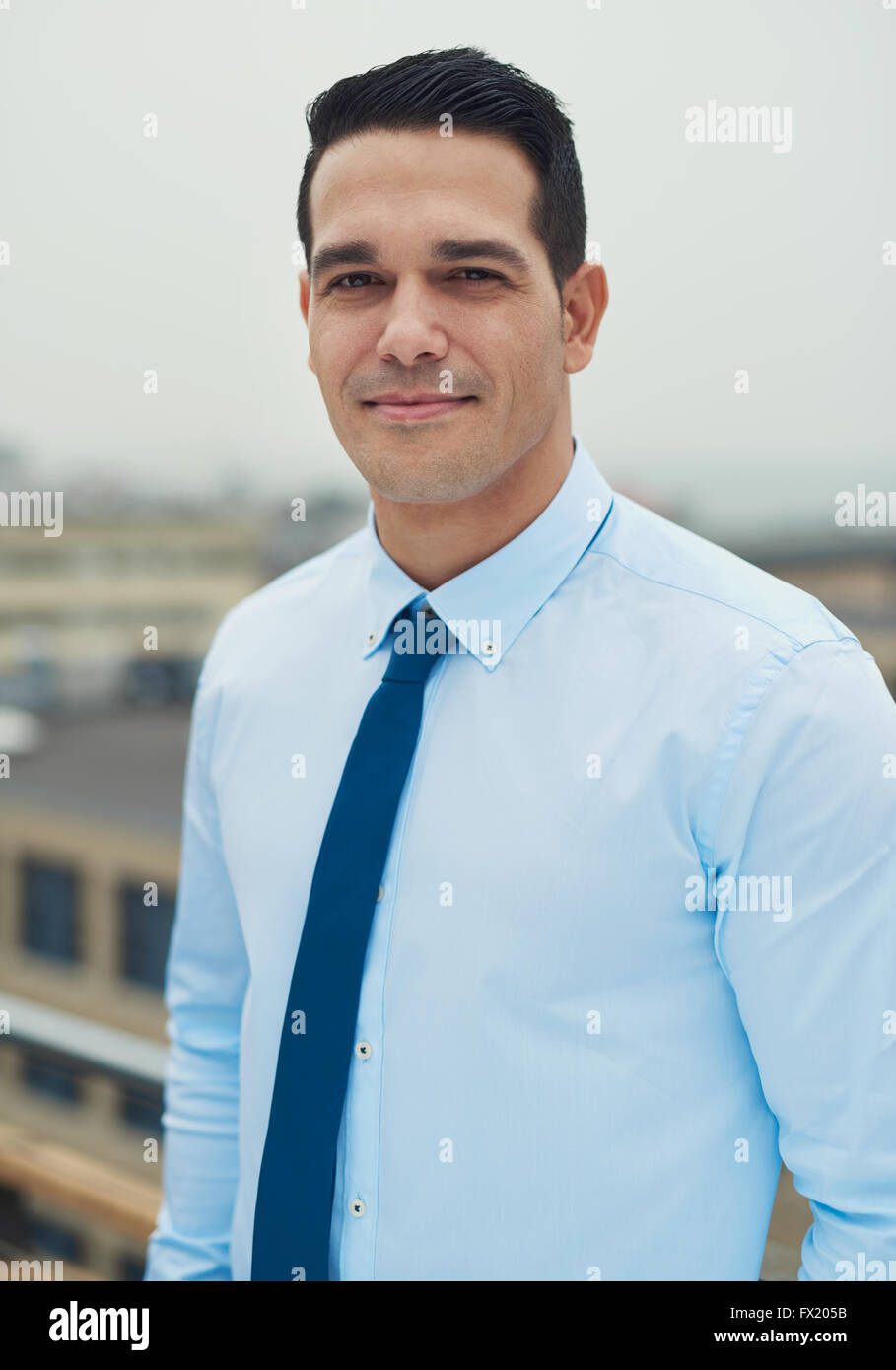 Young handsome Hispanic business man standing on a rooftop of an urban ...