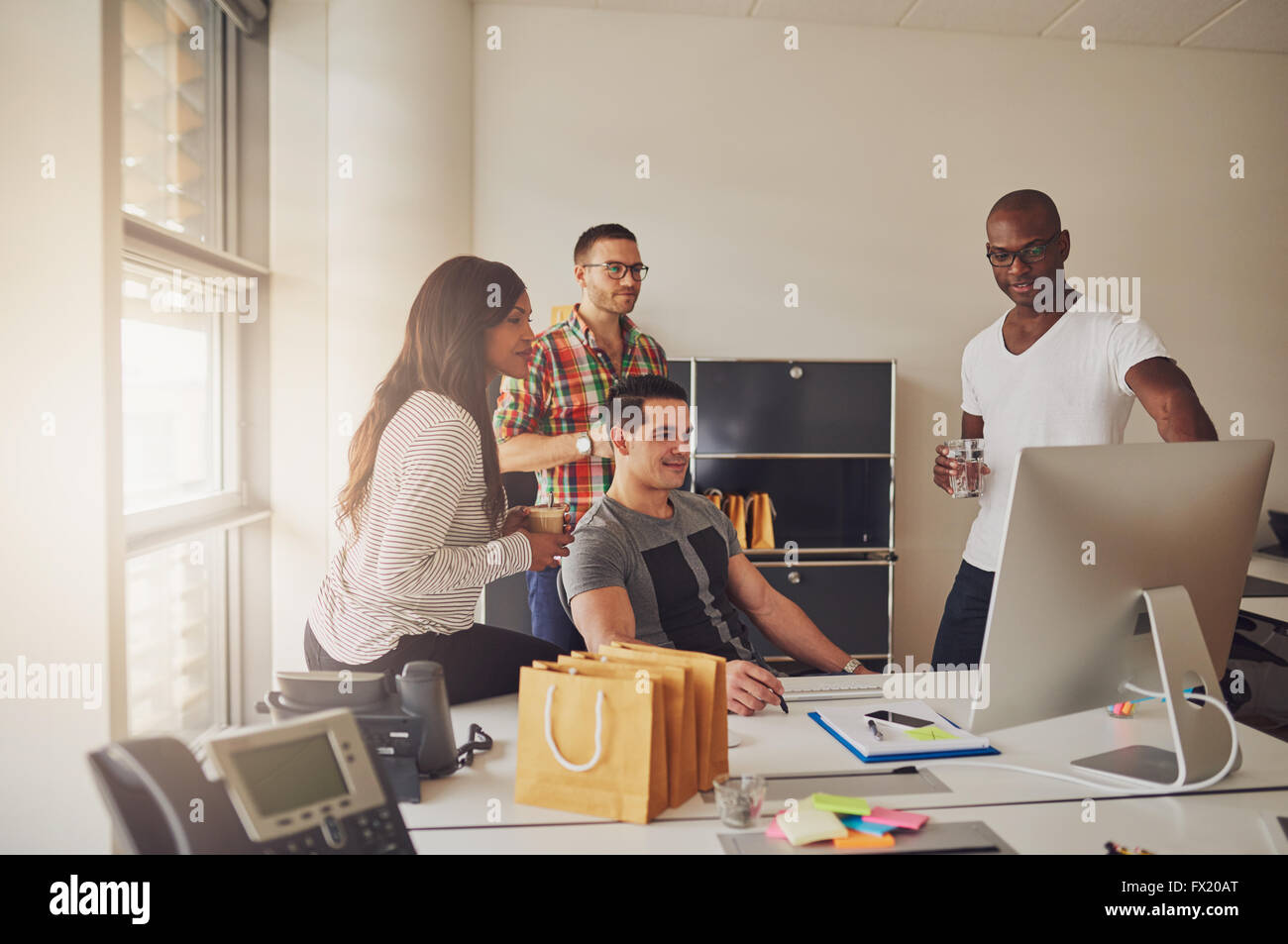 Four young adults sitting around desk with computer, telephone, sticky ...