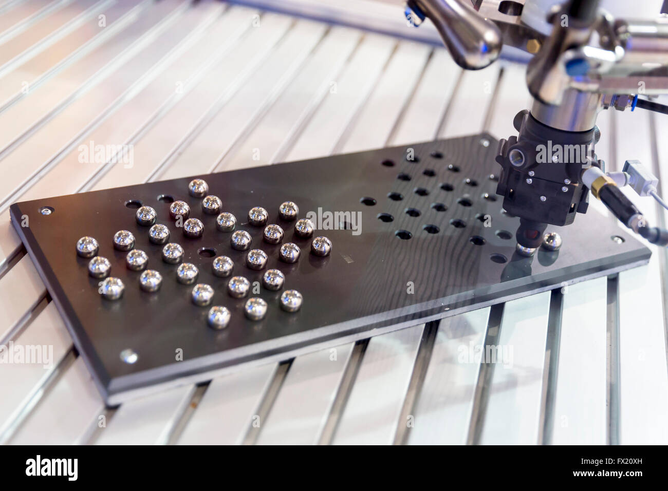 A robotic mechanical arm arranges small metal balls. The machine is ...