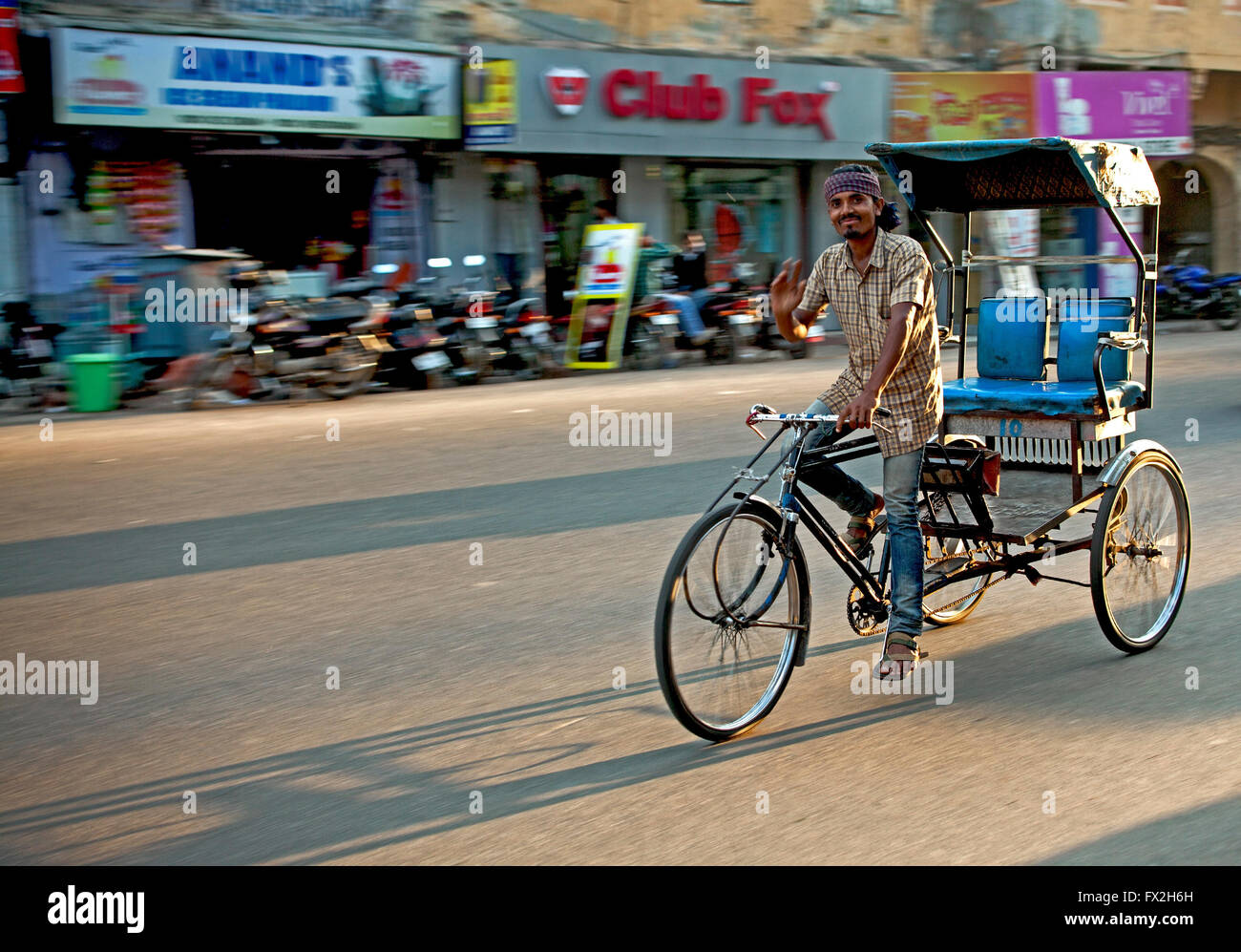 Rickshaw cyclist riding his rickshaw on a street in India at the end of ...