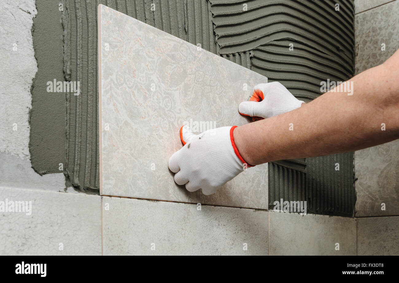 Tiler placing ceramic wall tile in position over adhesive Stock Photo ...