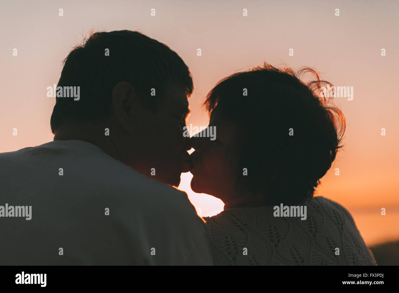 Adult married couple kiss against a sunset Stock Photo - Alamy