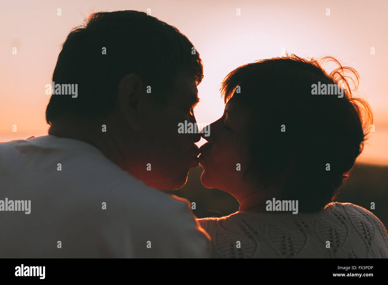 Adult married couple kiss against a sunset Stock Photo - Alamy