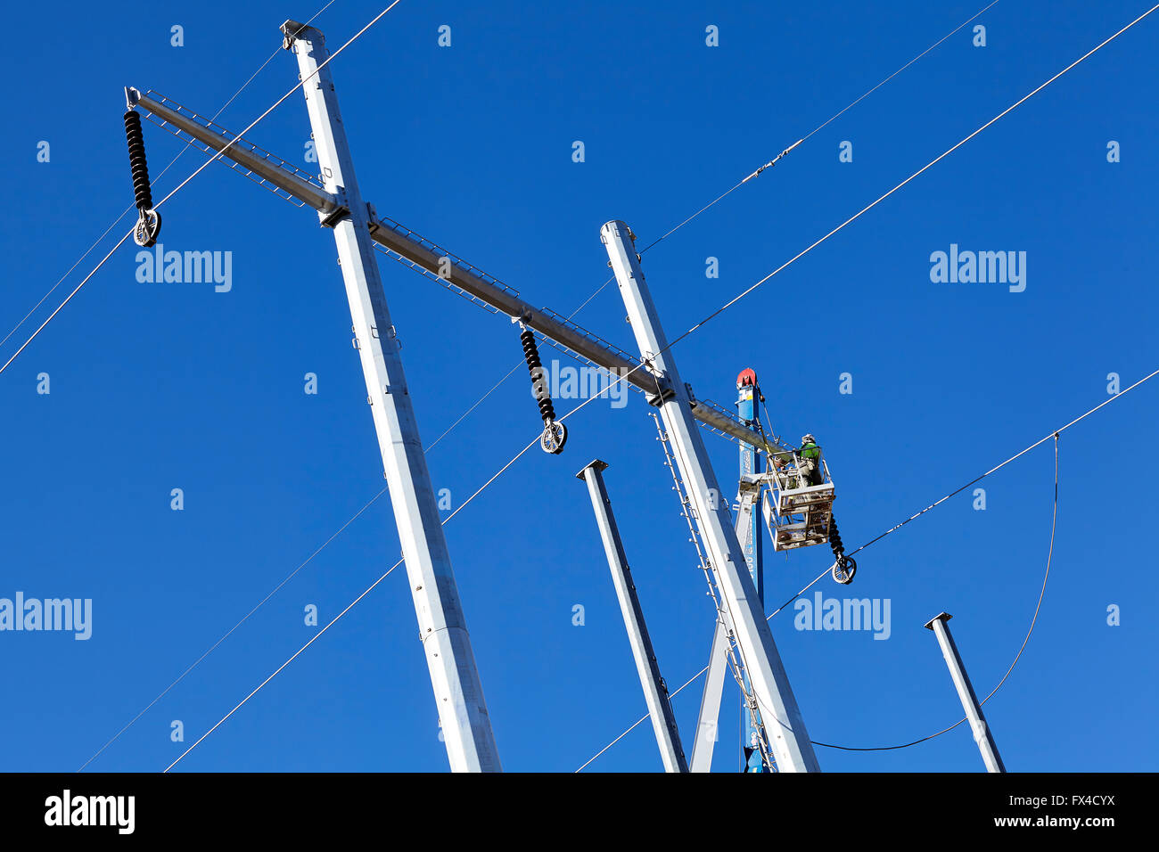 high voltage power line transmission tower workers with crane and blue ...