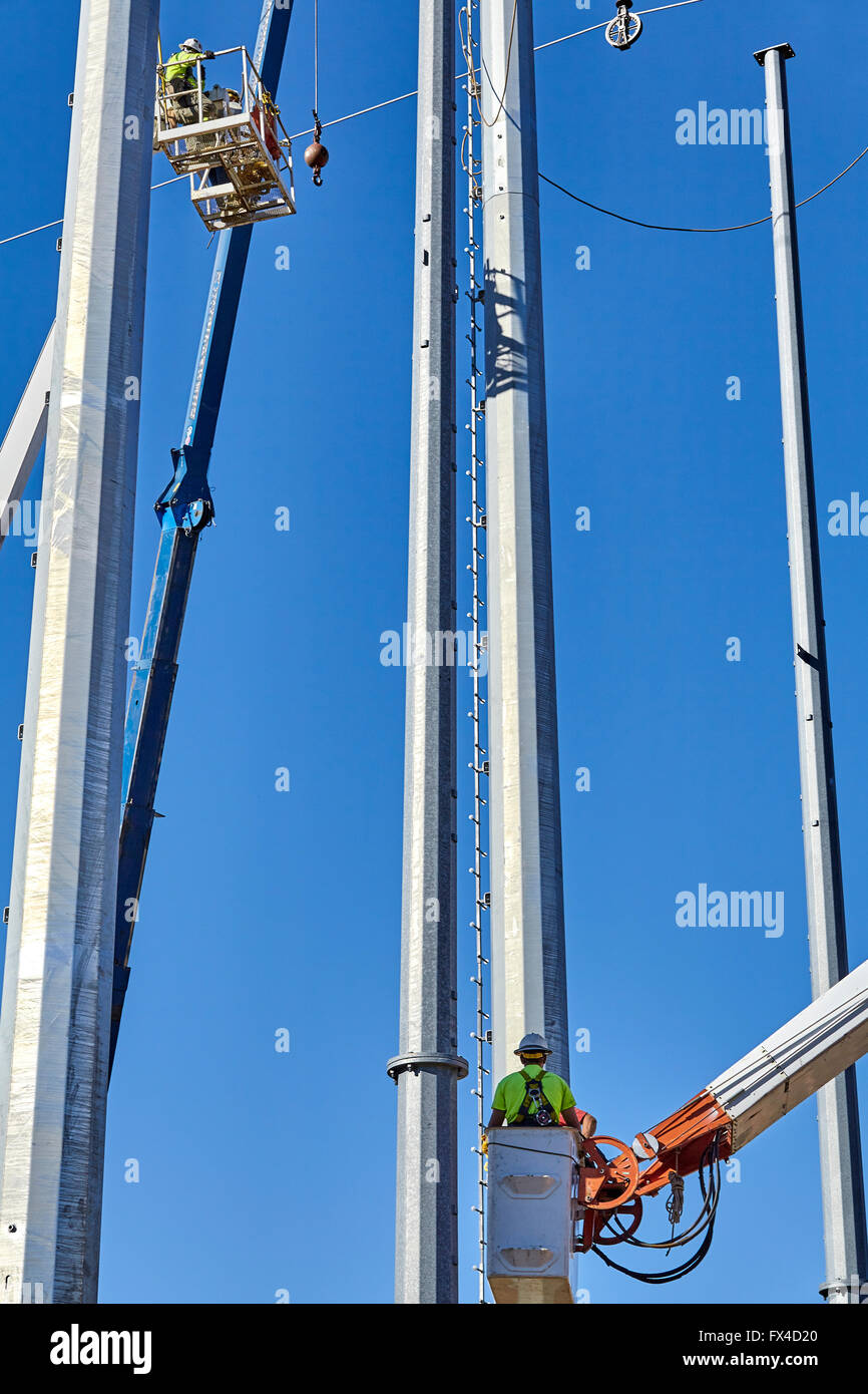 high voltage power line transmission tower workers with crane and blue ...