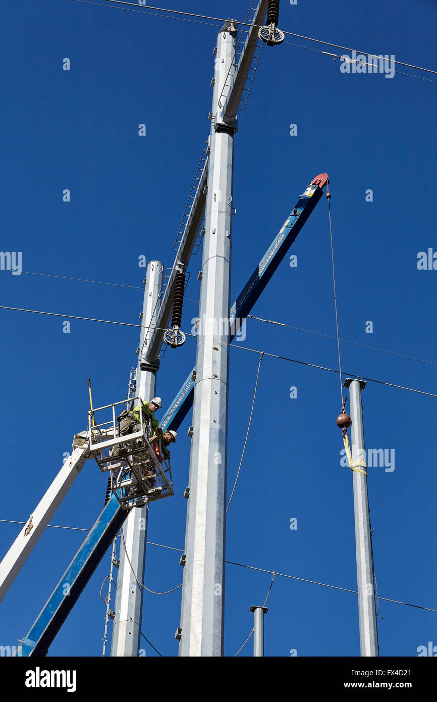 high voltage power line transmission tower workers with crane and blue ...