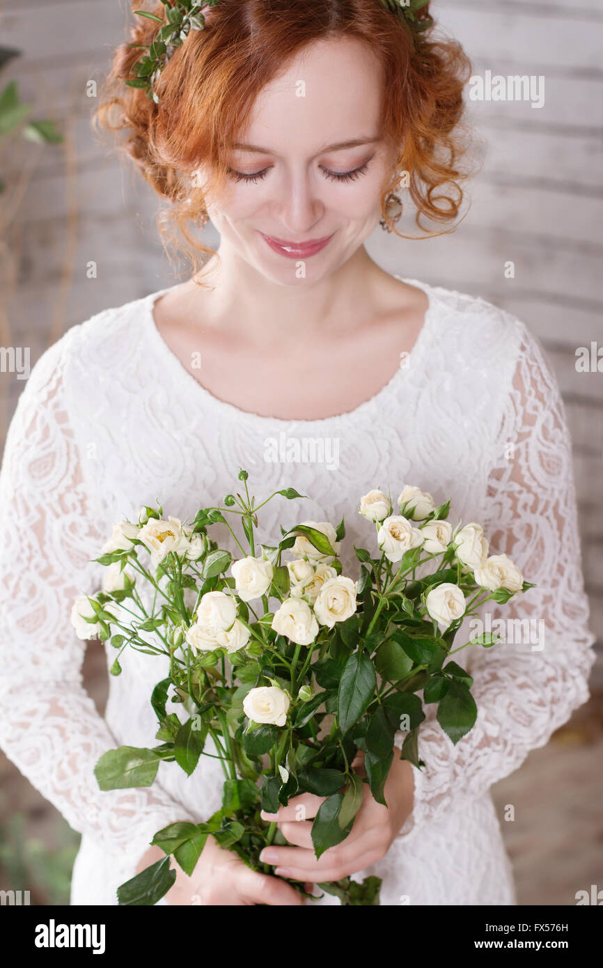 Portrait of a young red-haired bride in a simple lace dress with a ...