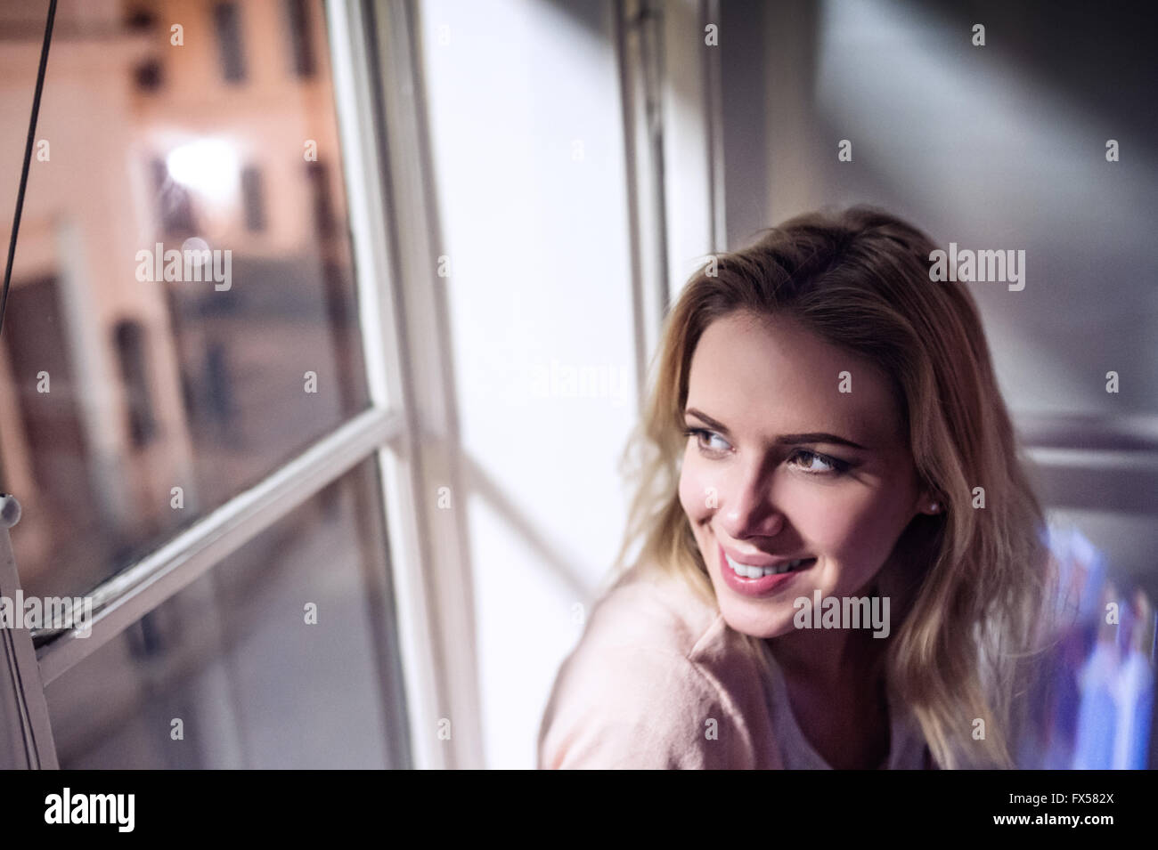 Woman sitting on windowsill, looking out of window, smiling Stock Photo ...