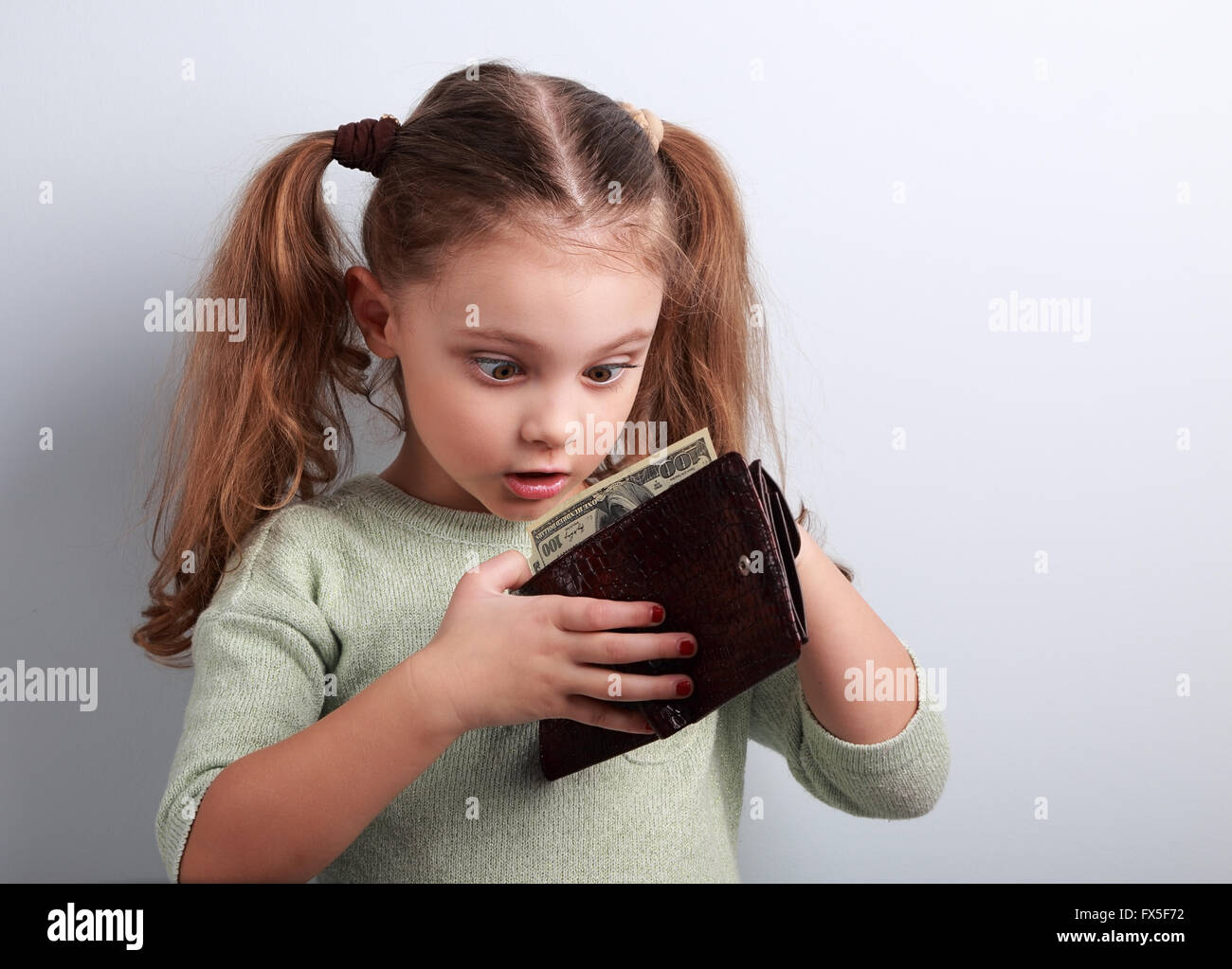 Cute surprising kid girl holding and looking in wallet with dollars ...