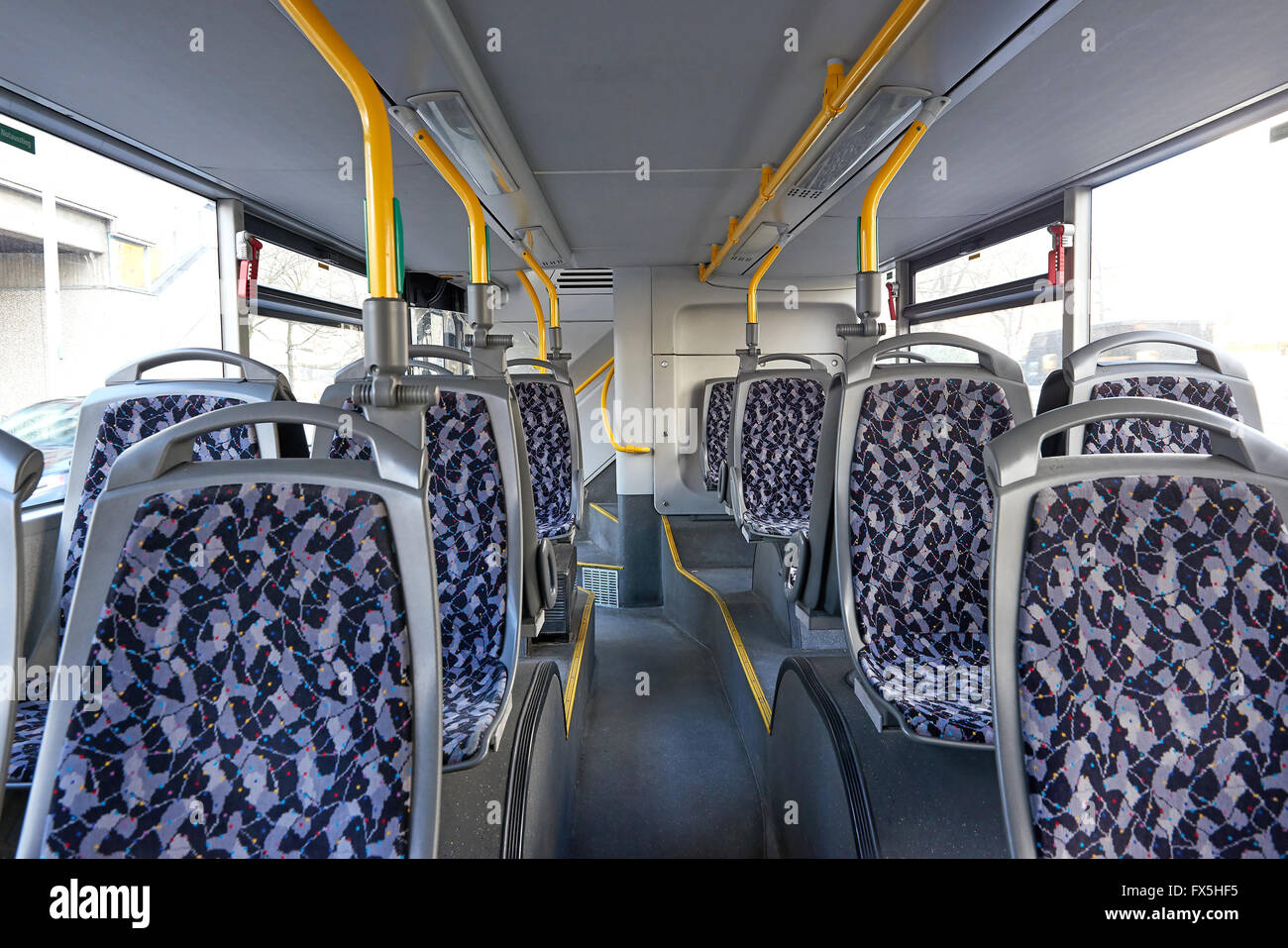 Empty bus seats with a blue pattern and yellow handlebars above them ...