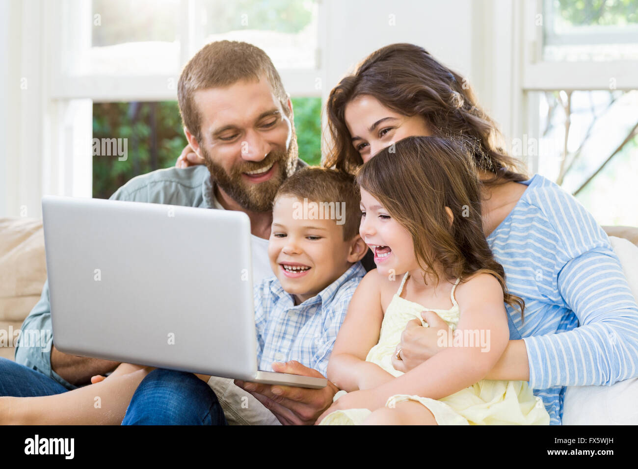 Parents and kids using laptop in living room Stock Photo - Alamy