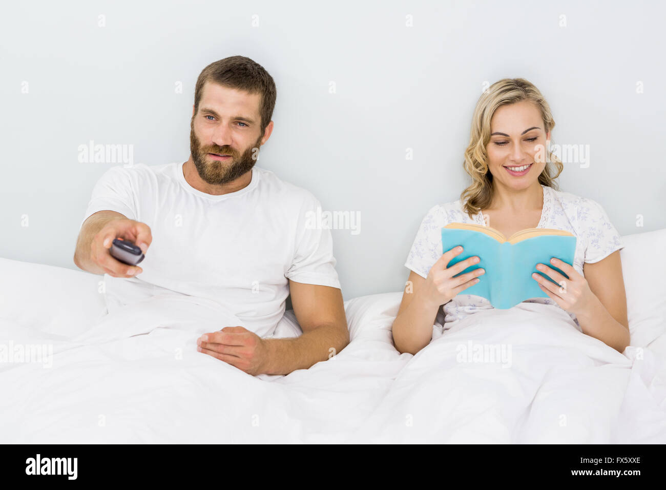 Man watching television while woman reading book Stock Photo - Alamy