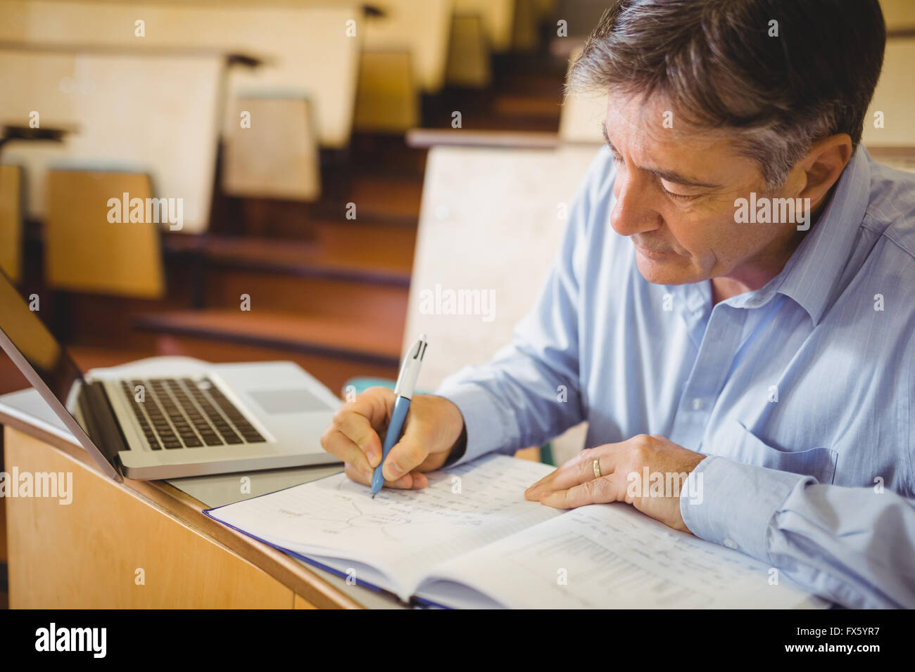Professor writing in book at desk Stock Photo - Alamy