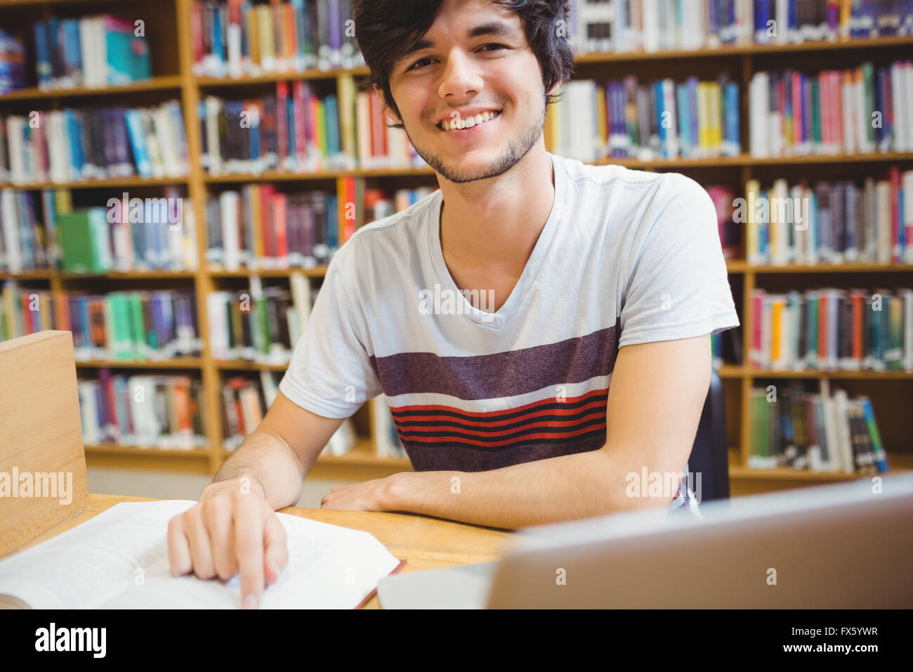 Happy young student sitting at desk reading a book Stock Photo - Alamy