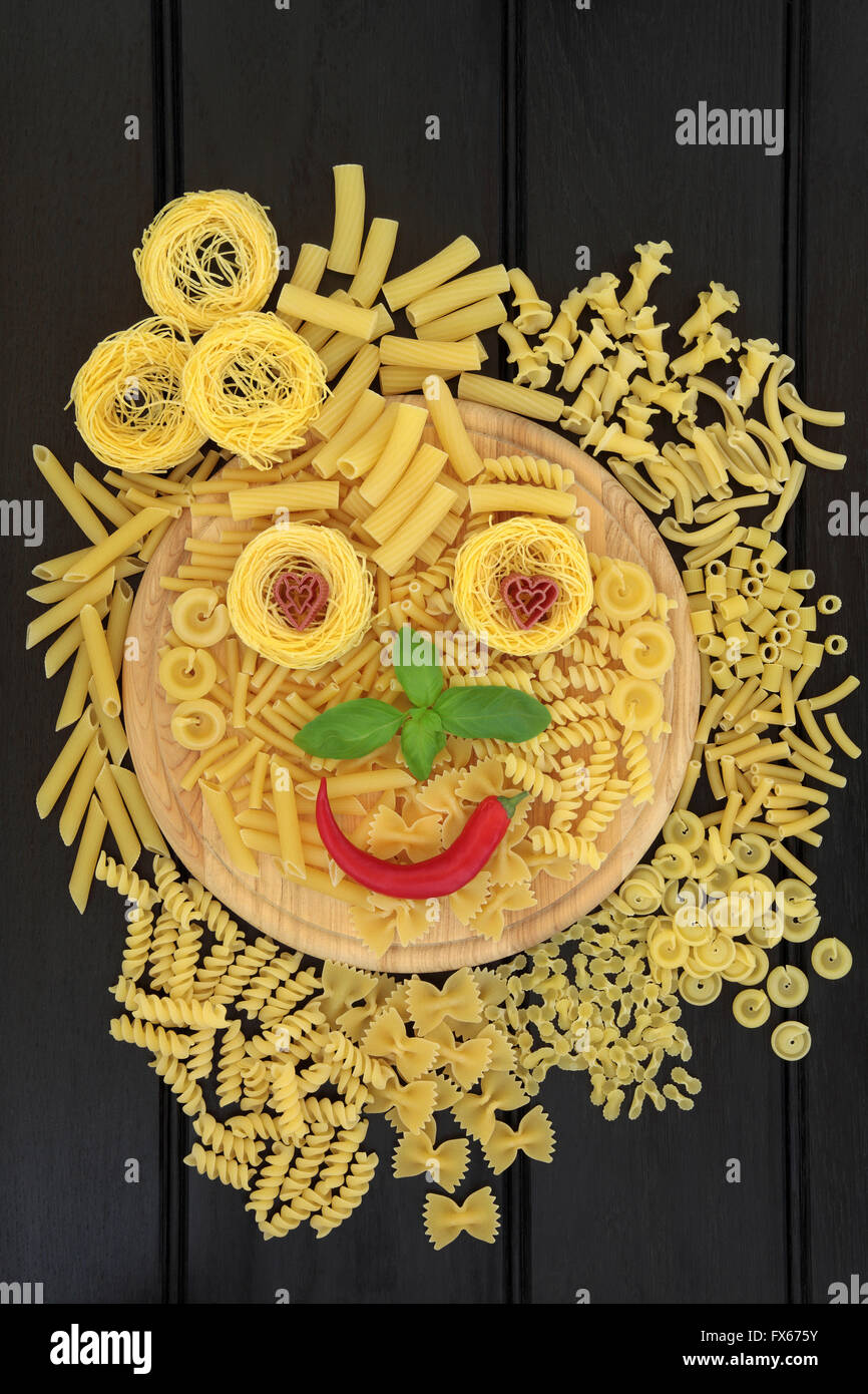 Pasta selection with abstract smiley face on a wooden board over dark ...