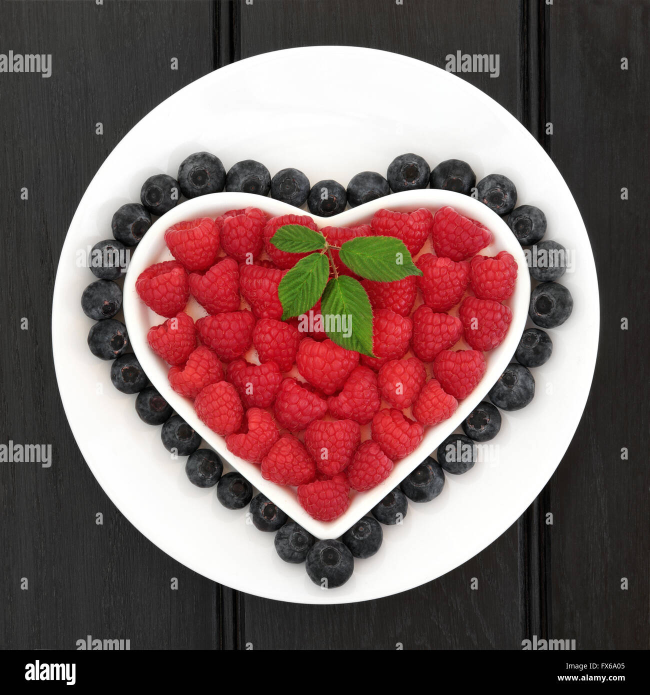 Raspberry and blueberry fruit in a heart shaped bowl on a white round ...