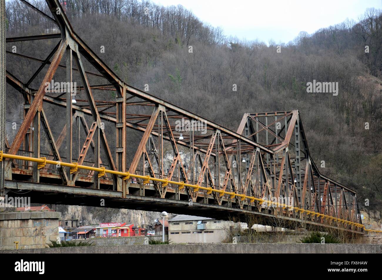 Old Yugoslav rusty metal bridge across river with yellow pipe to town ...