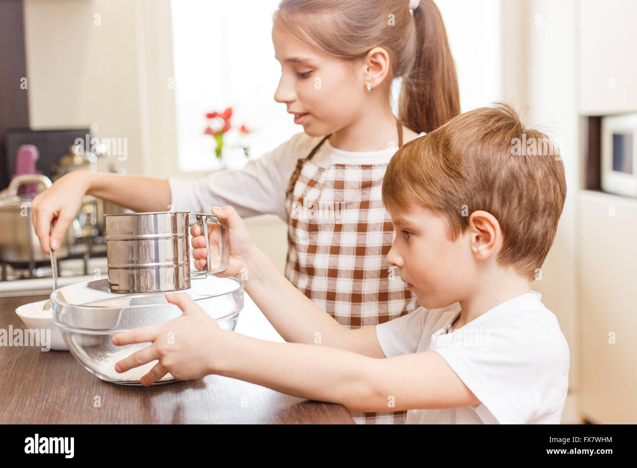Small girl with her brother put flour into the sieve. Children cooking ...