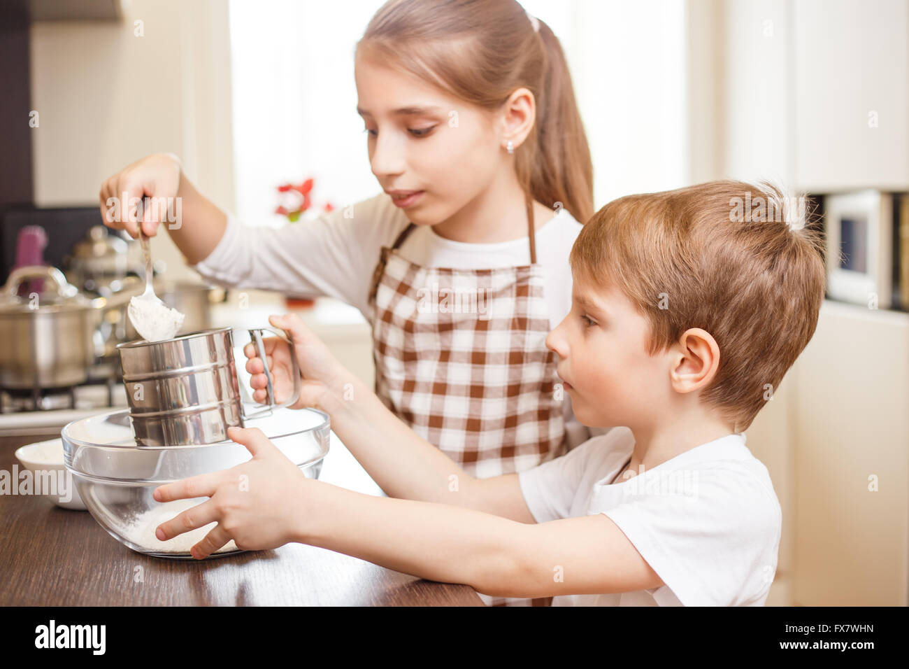 Small girl with her brother put flour into the sieve. Children cooking ...
