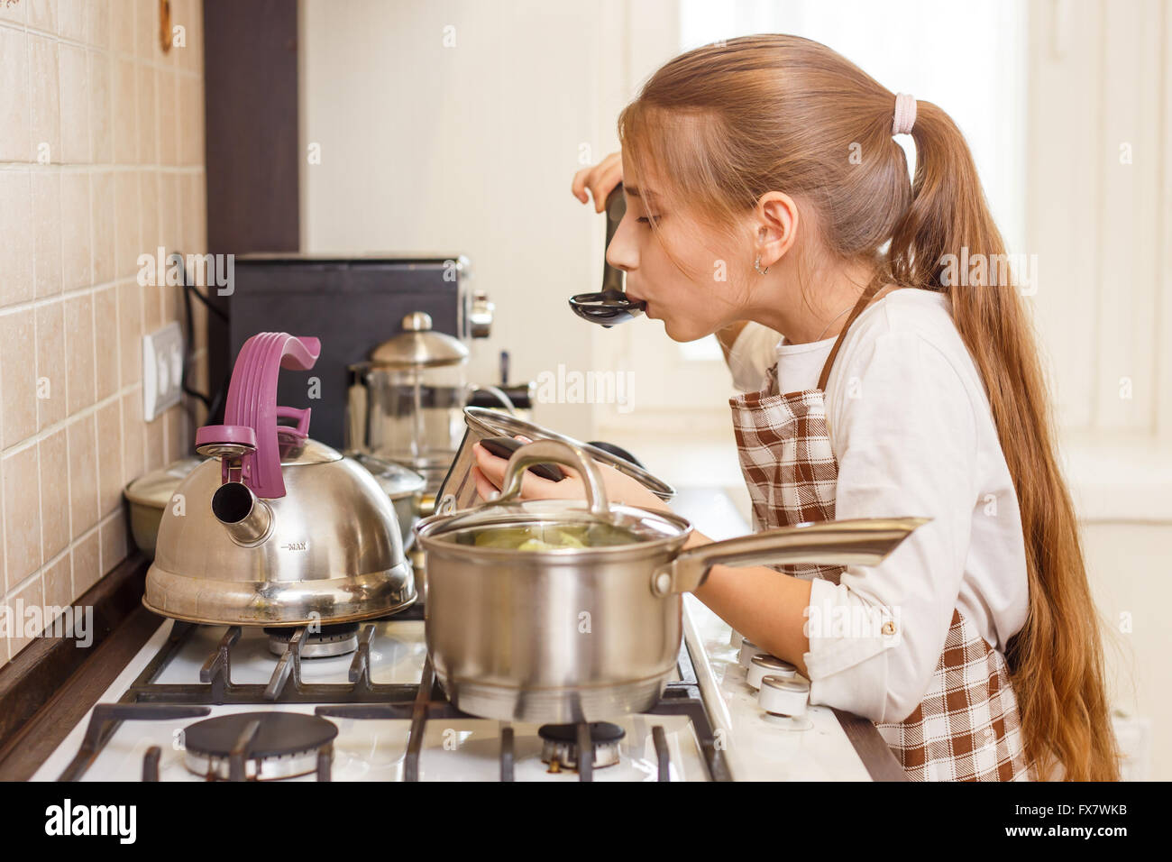 Small teenage girl cooking in the home kitchen. Caucasian cooking girl ...