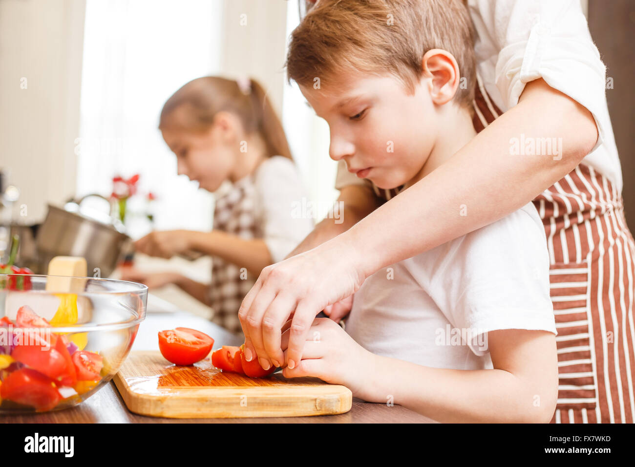 Small boy cutting in slices vegetables for salad with his mother in the ...