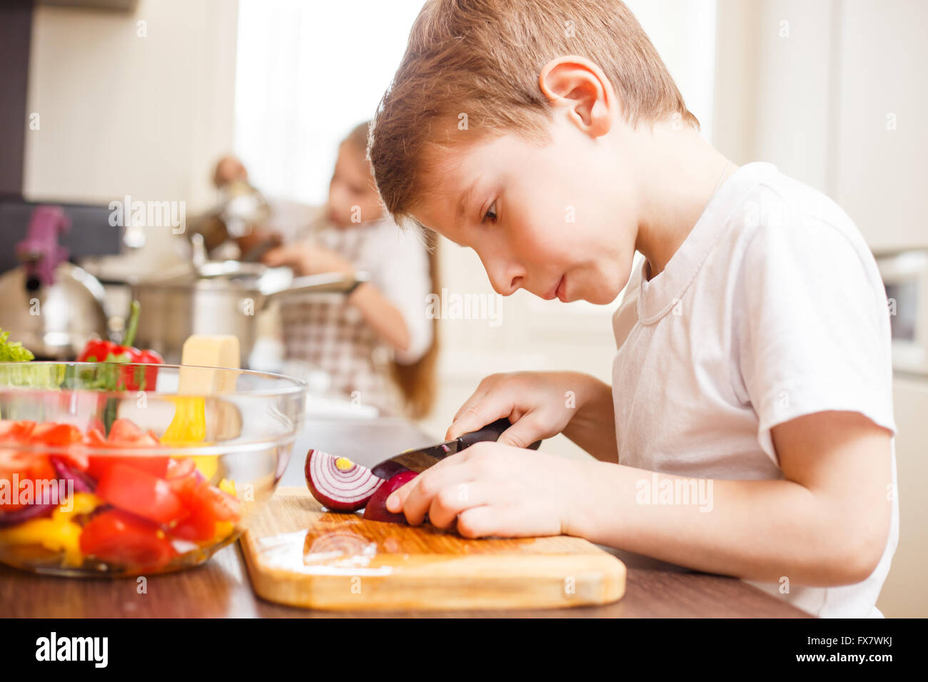 Small boy cooking together with his sister. Cute boy cutting onion for ...