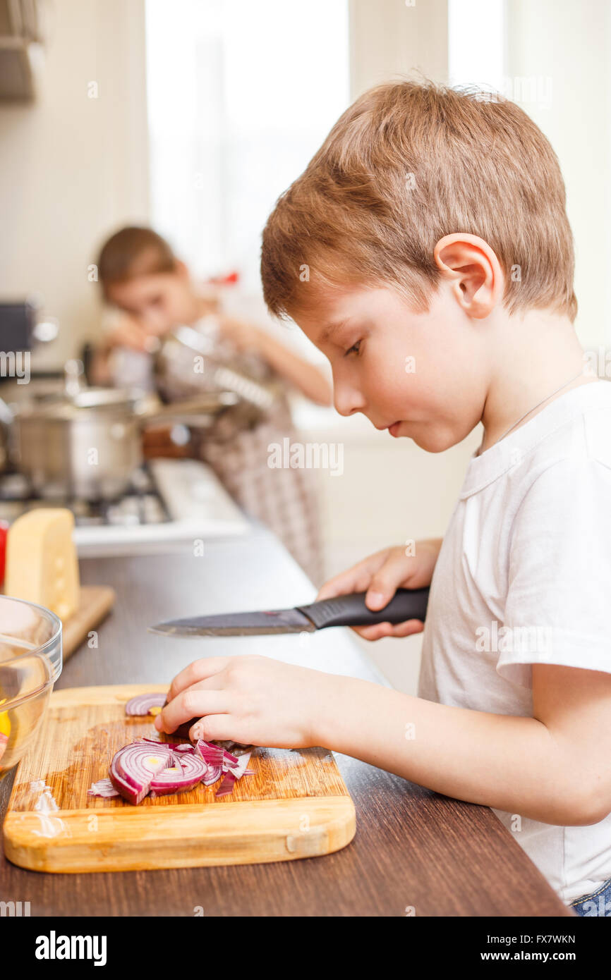 Small boy cooking together with his sister. Cute boy cutting onion for ...