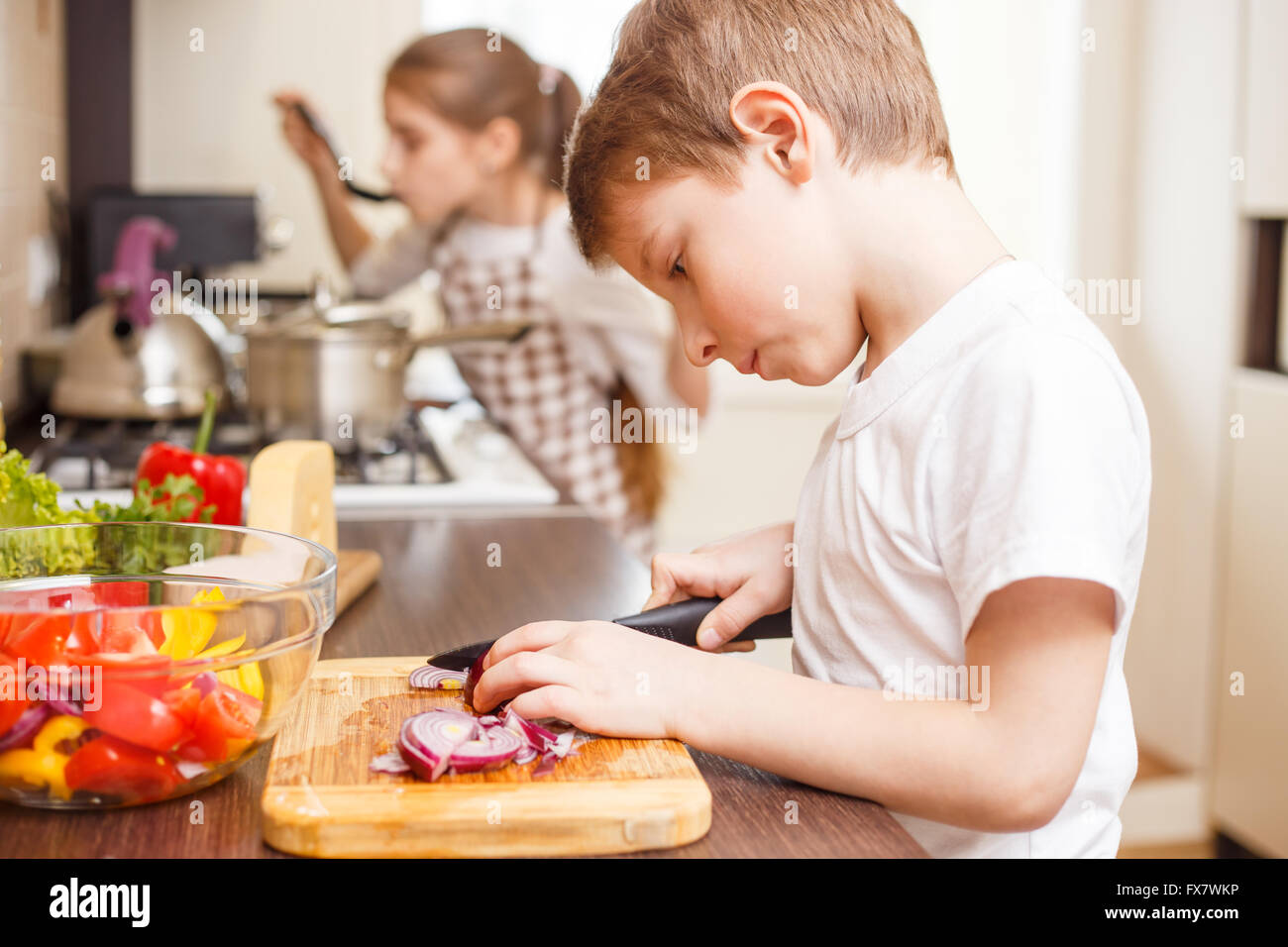 Small boy cooking together with his sister. Cute boy cutting onion for ...
