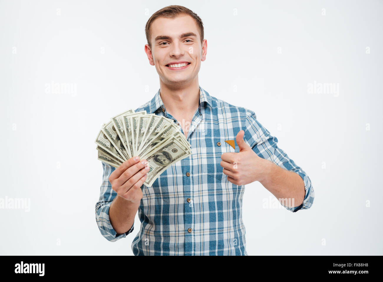 Cheerful successful young man holding money and showing thumbs up over ...